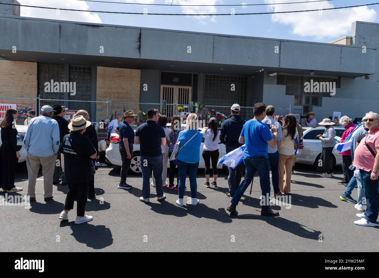 A crowd gathers to place flowers in the temporary fence at the burnt Adass Israel Synagogue ...