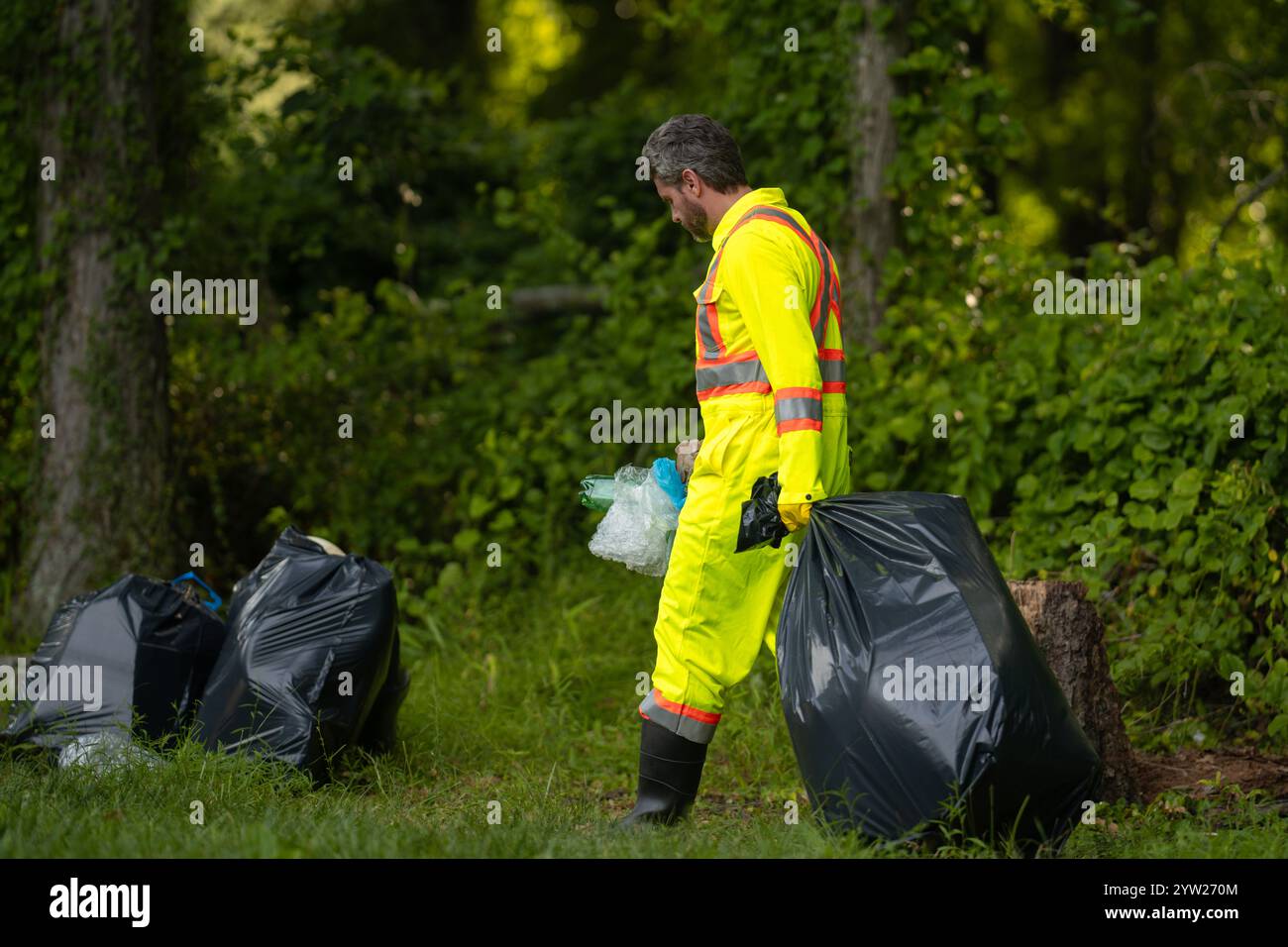 Volunteer man collecting garbage, picking up waste at nature. Land pollution, environmental ...