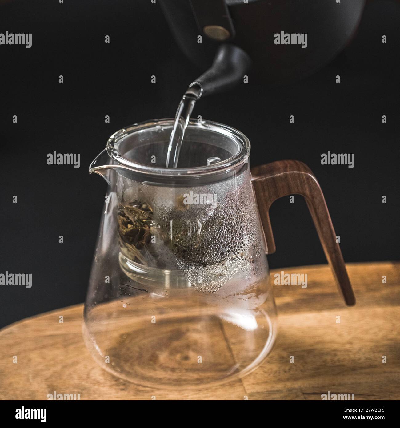 A stylish glass teapot pouring hot water for tea preparation, featuring ...