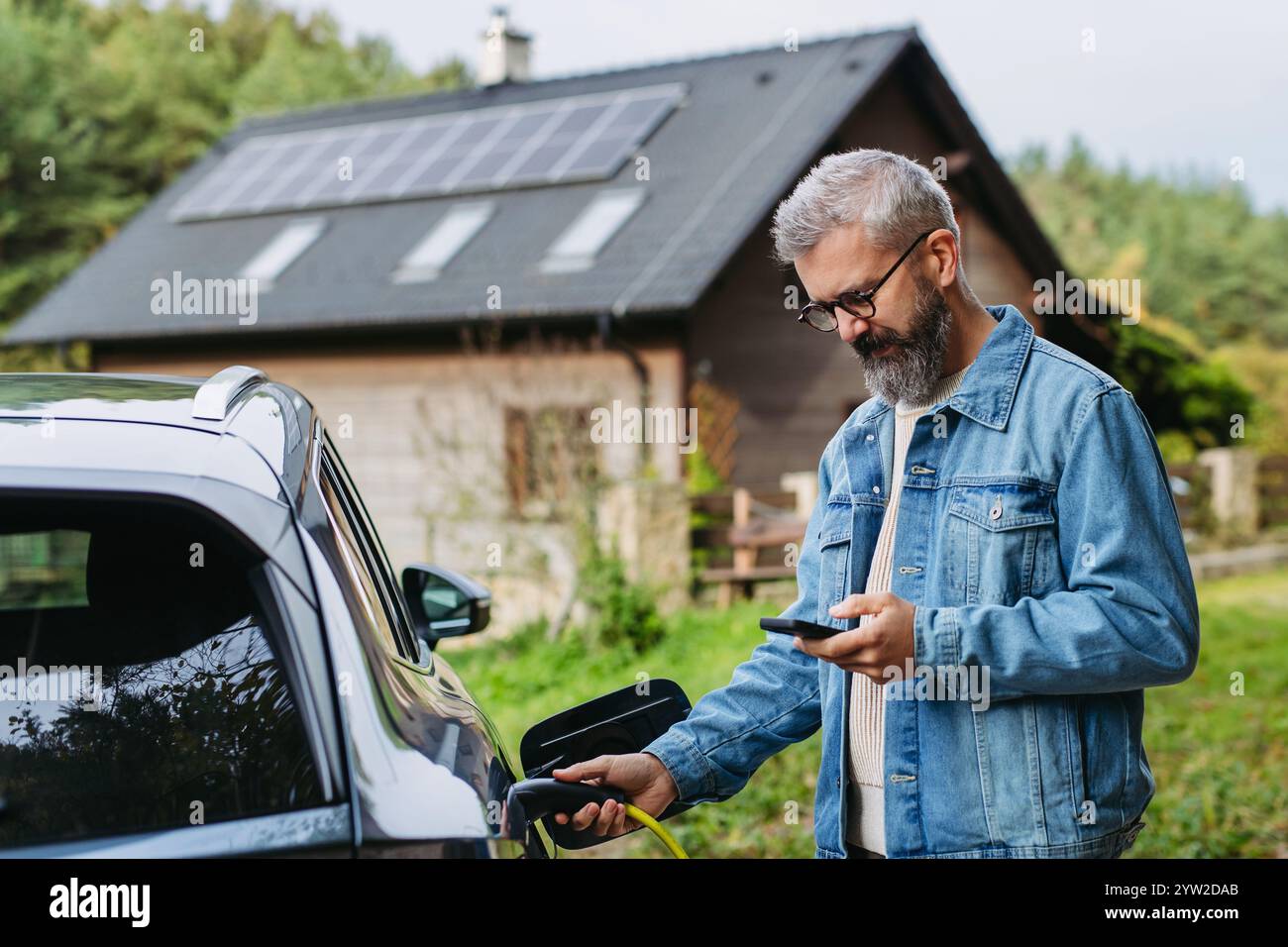 Man charging electric car in front of his house, plugging the charger ...