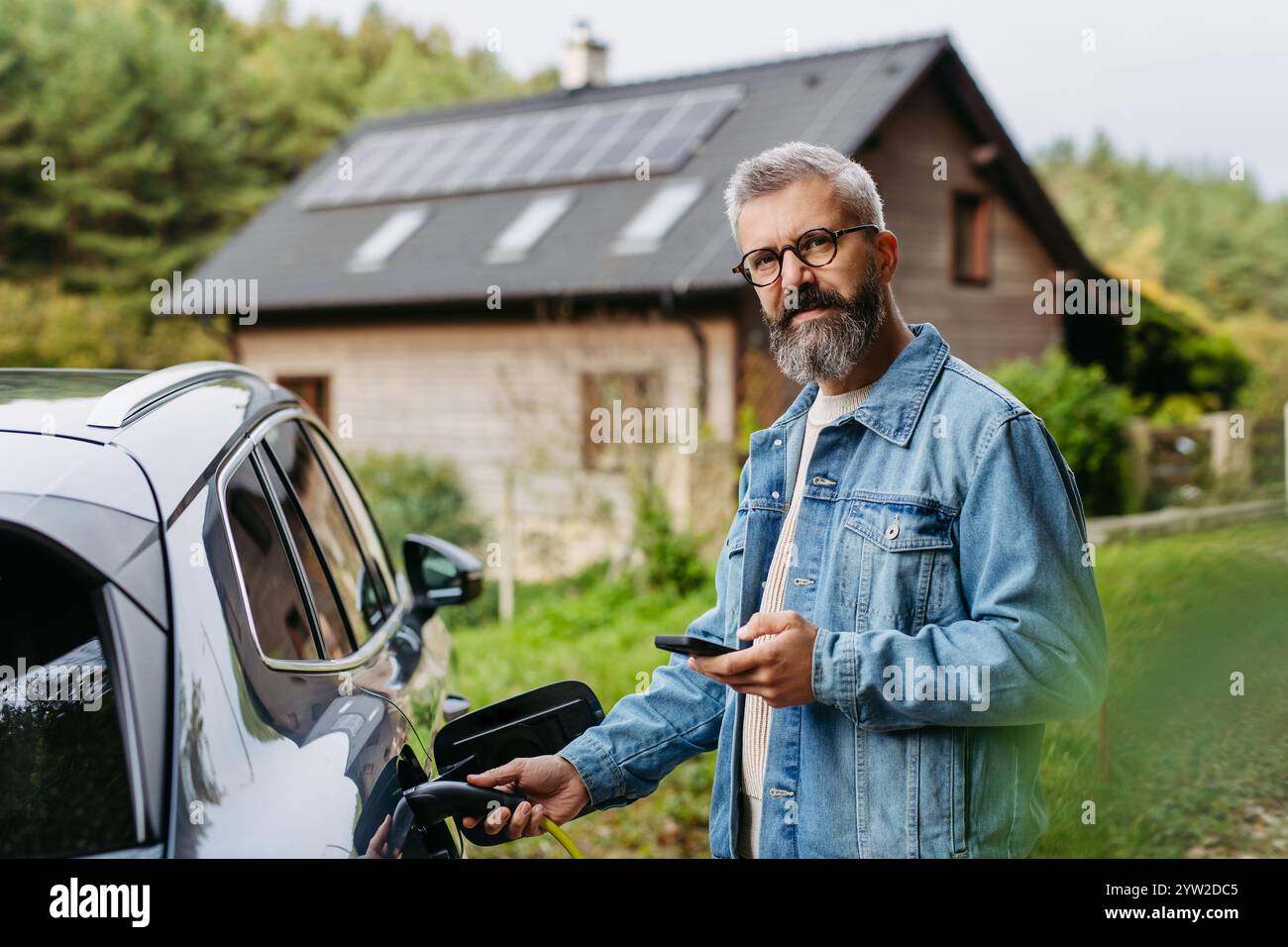 Man charging electric car in front of his house, plugging the charger ...