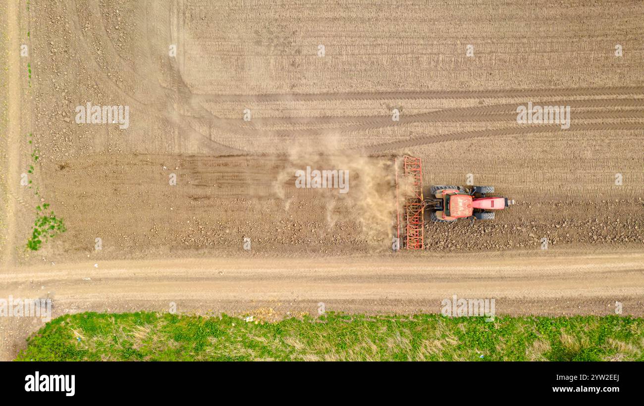 Above top view of tractor as pulling machine, harrowing arable field ...