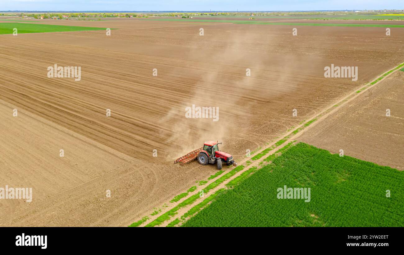 Above top view of tractor as pulling machine, harrowing arable field ...