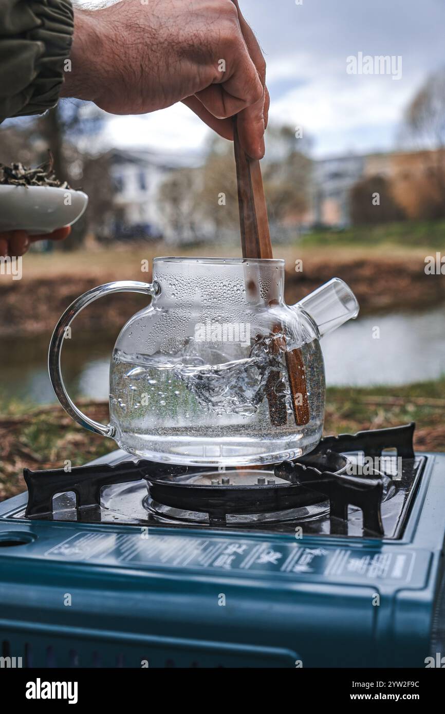 A hand is stirring the boiling water inside a kettle while outdoors ...