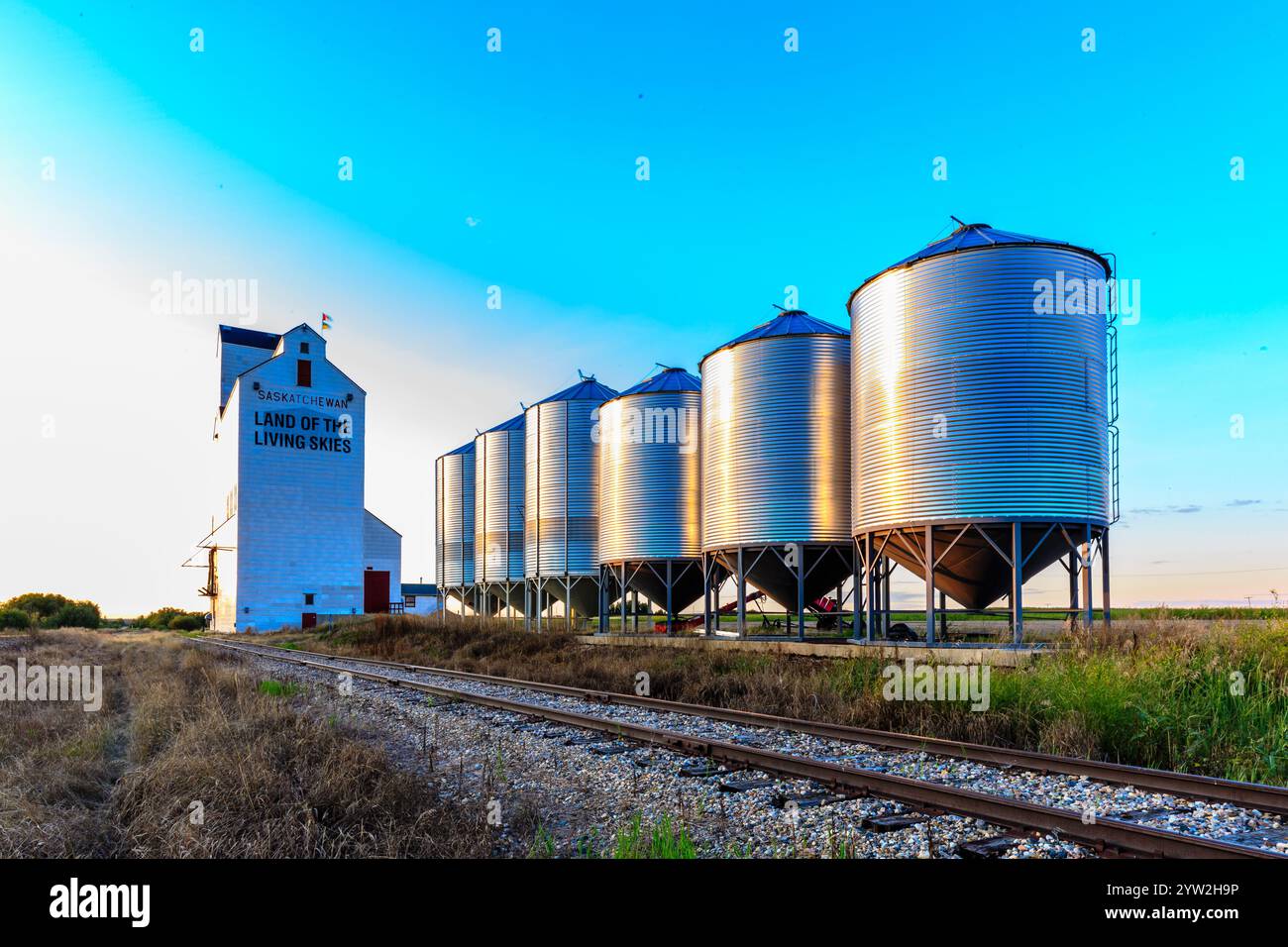 A row of silos are in front of a grain silo. The silos are silver and ...
