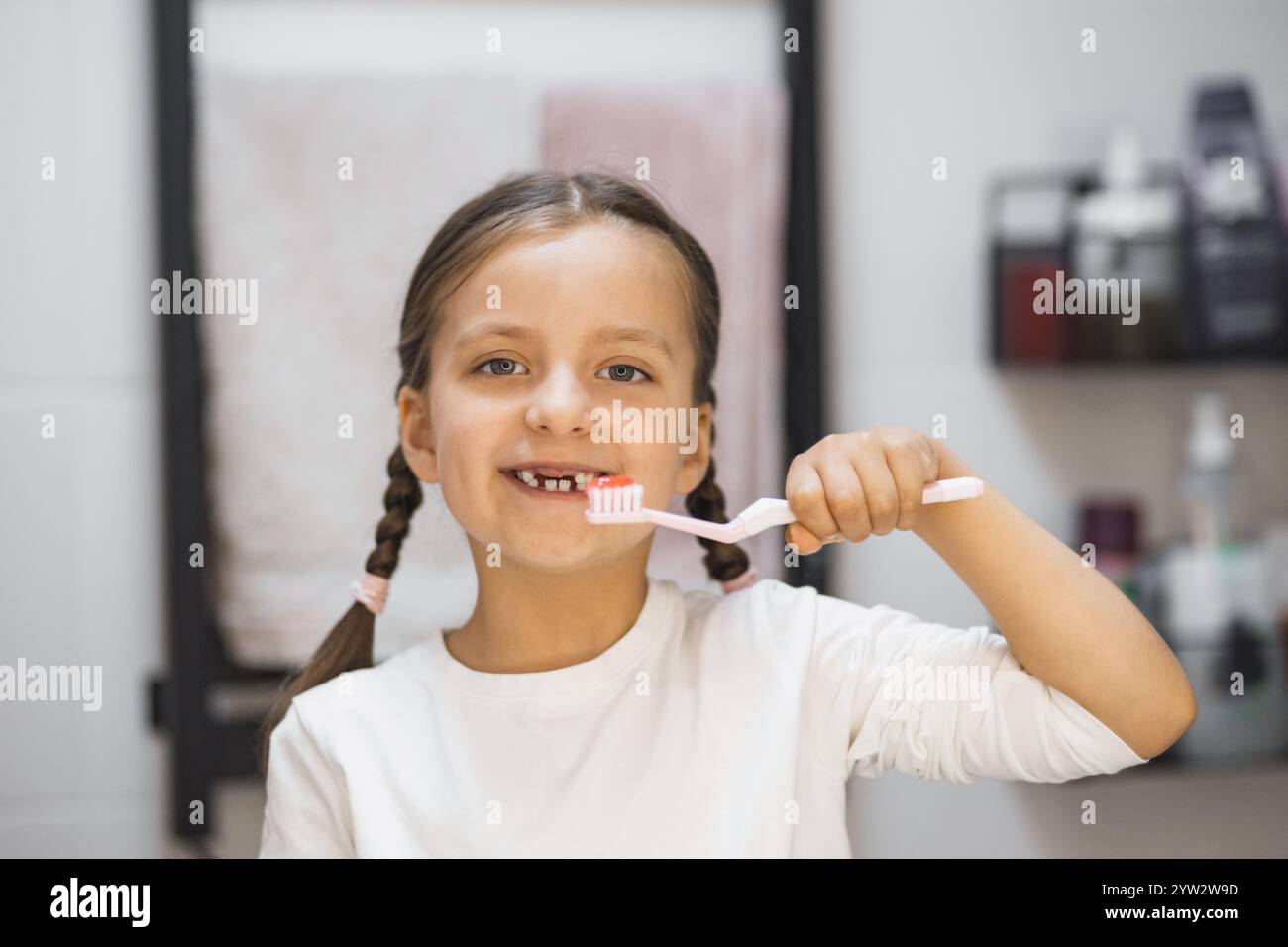 Caucasian girl with braided hair brushing her teeth and smiling at ...