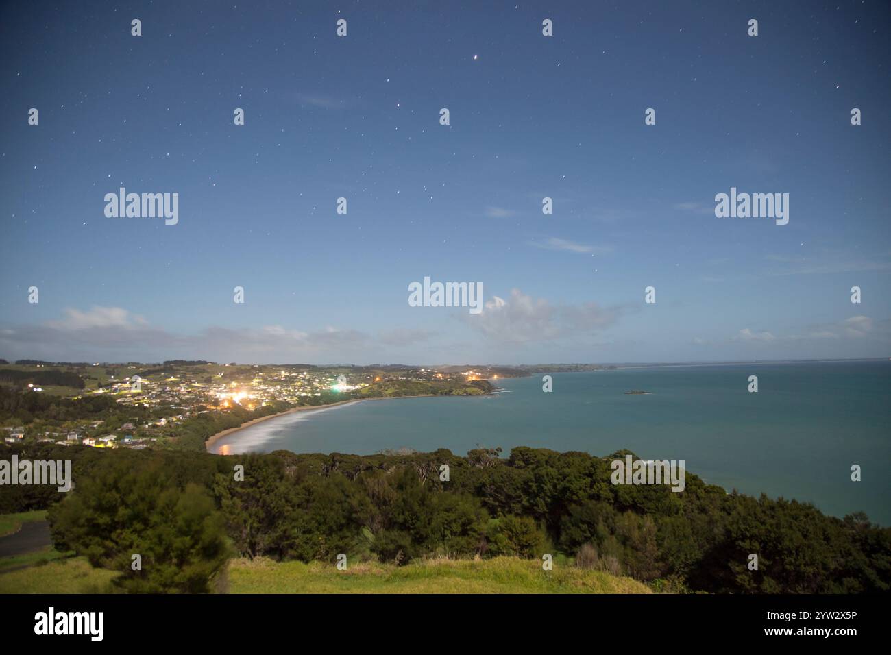 Coastal town at night with a starry sky and illuminated streets ...