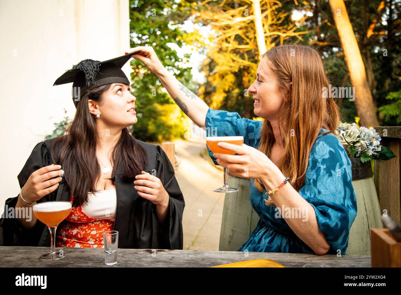 Graduate in cap holding a cocktail smiles at a woman in a blue dress at ...