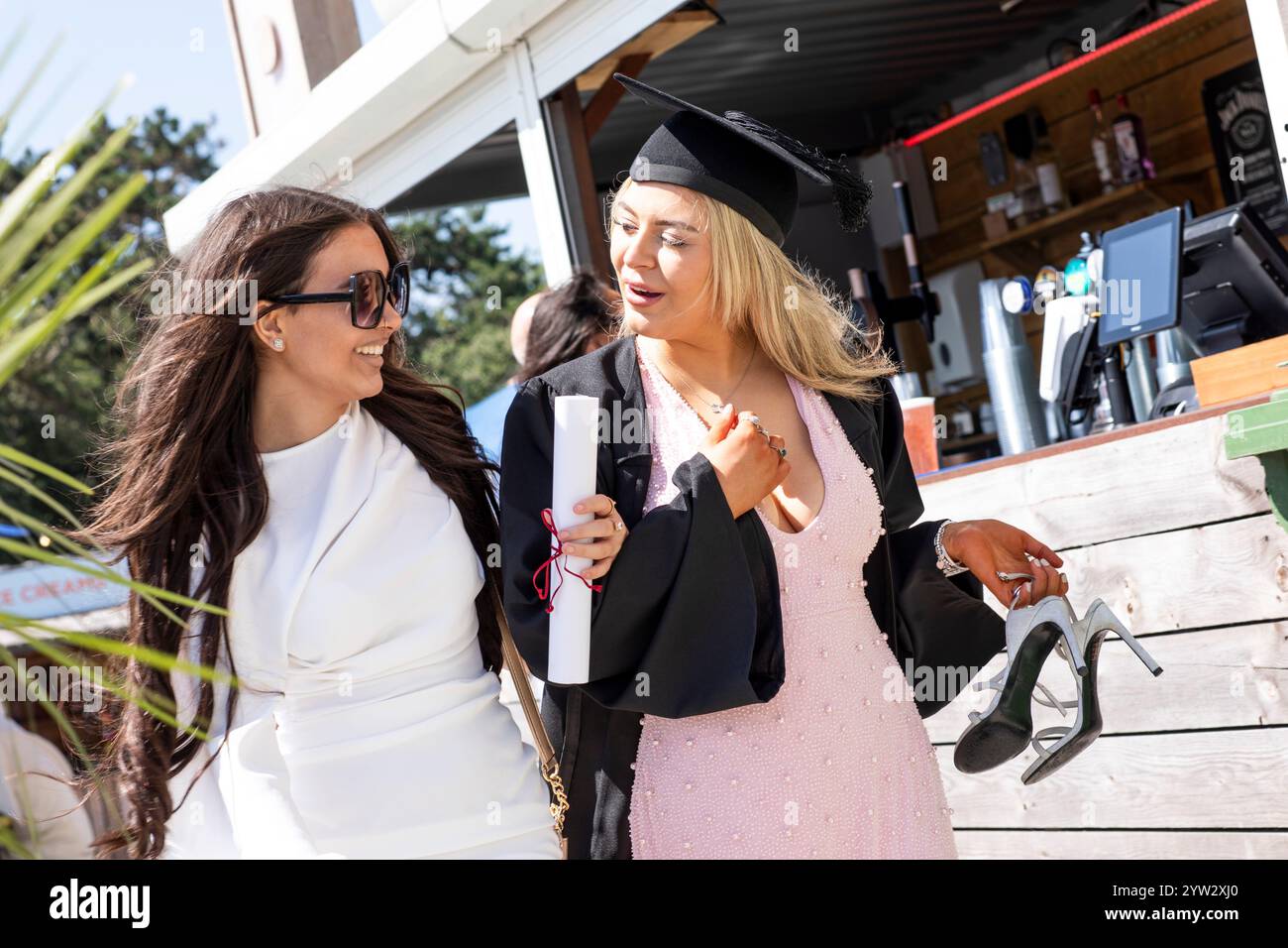 Smiling woman in graduation cap and gown walking and talking with a ...