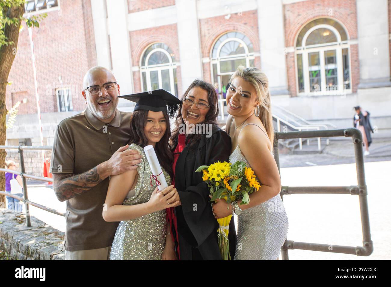 Smiling family celebrating a young woman's graduation outside a brick ...