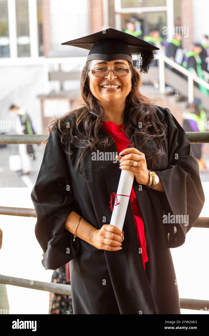 Smiling woman in graduation attire holding a diploma, standing proudly ...