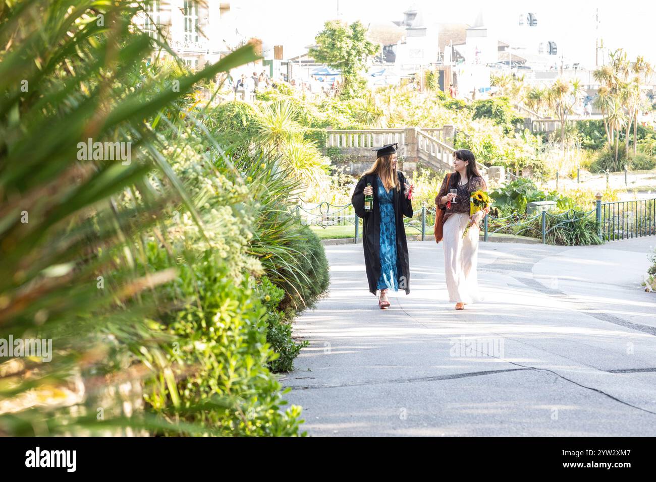 Two young women in graduation attire walk and converse on a sunny ...