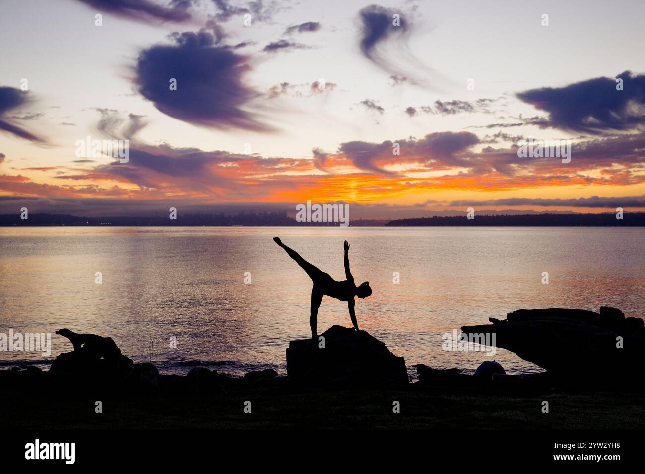 Silhouette of a woman performing a handstand on a rock by the sea at ...