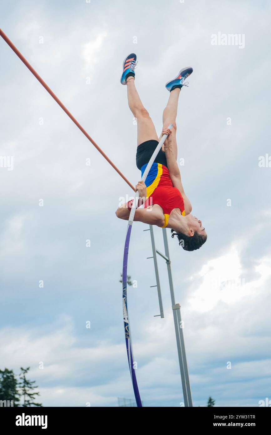 Female athlete performing a high pole vault against a cloudy sky ...