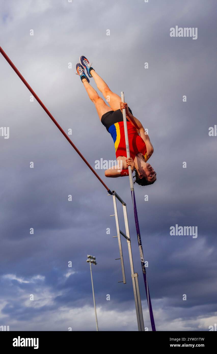 Female athlete performing a high pole vault against a cloudy sky ...
