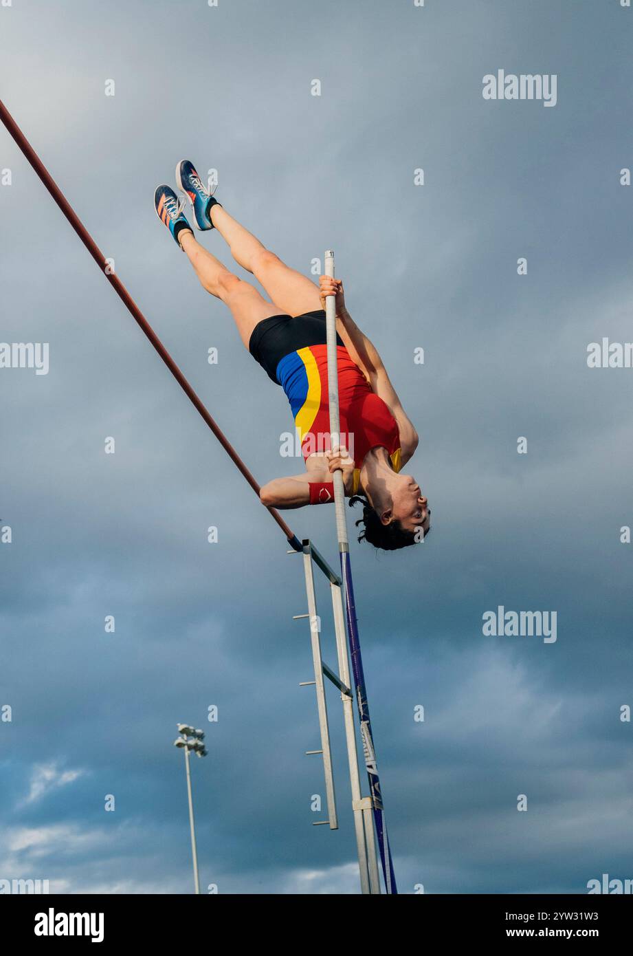 A female athlete in a red top and multi-colored shorts performs a pole ...