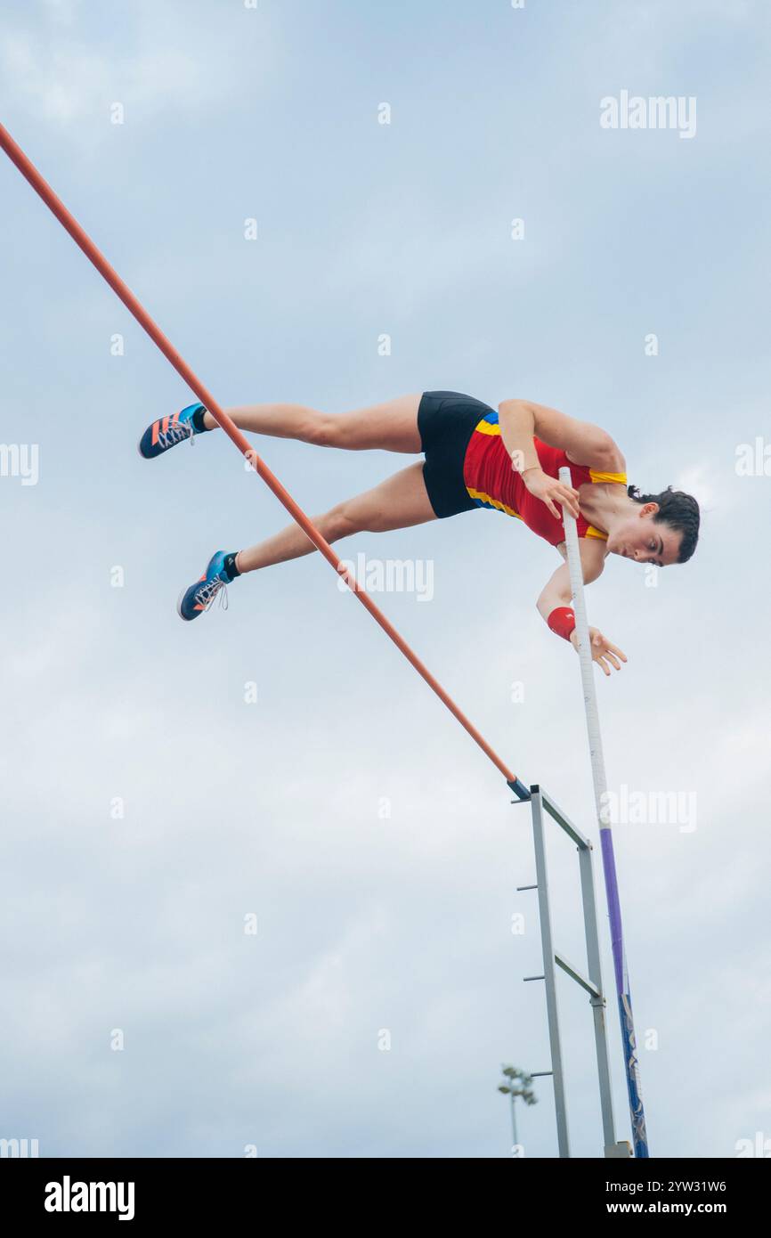 Female pole vaulter in mid-air clearing the bar against a cloudy sky ...