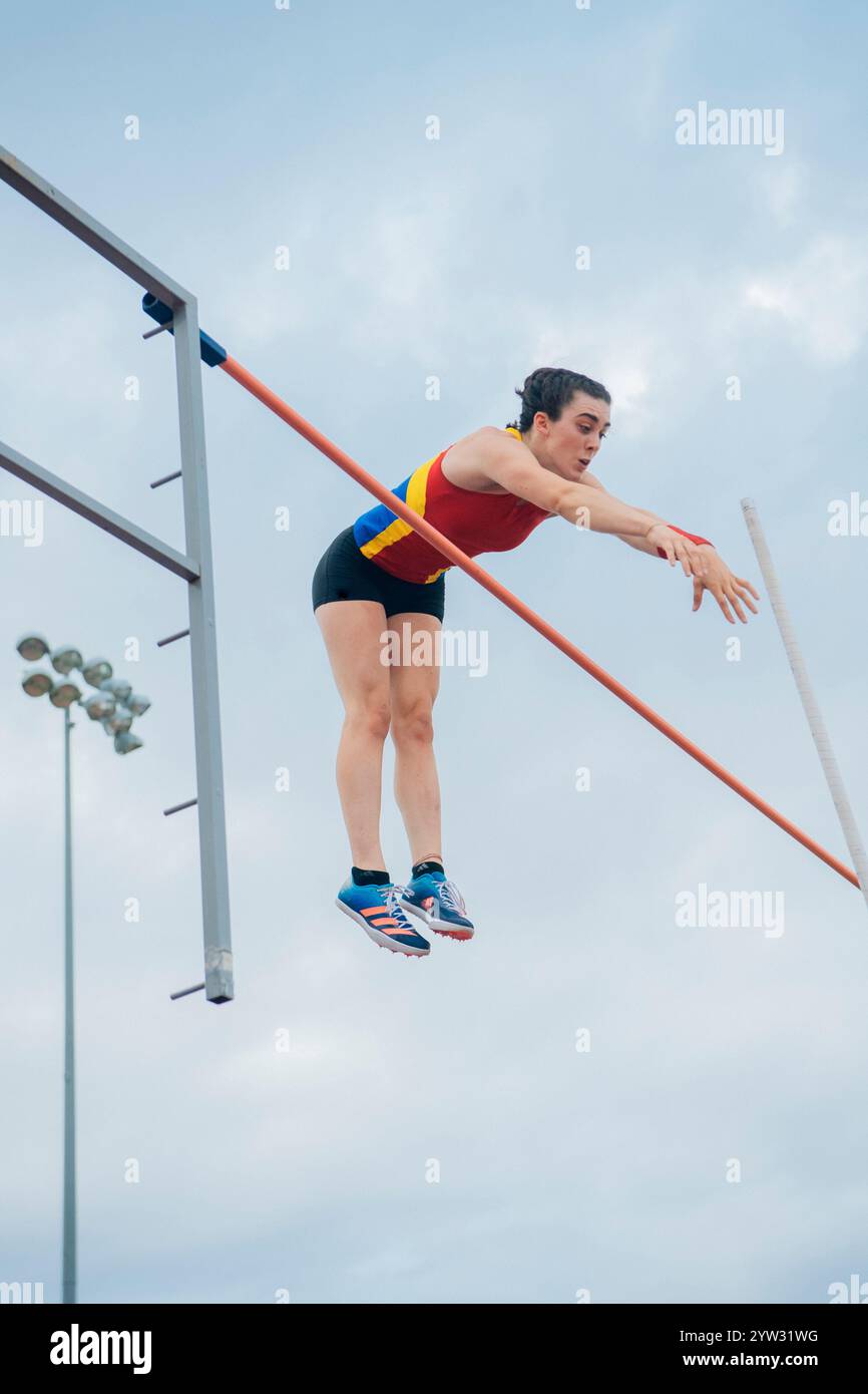 Female athlete vaulting over the bar during a pole vaulting event under ...
