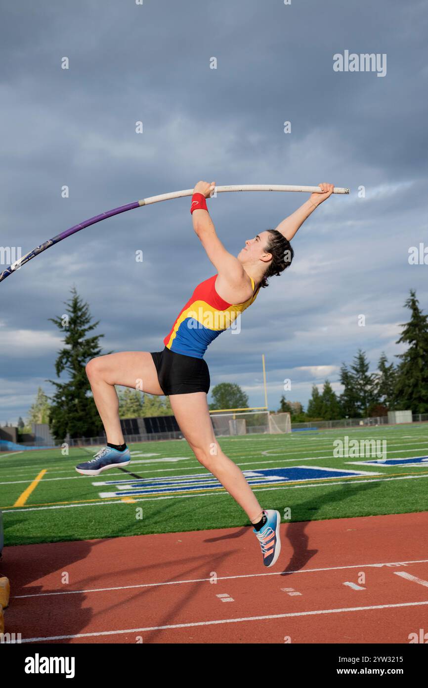 Female athlete in mid-action performing a pole vault jump against a ...