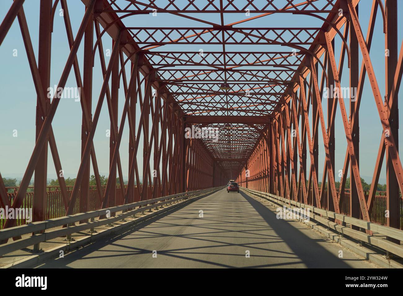 Red steel truss bridge with a single car driving over it on a clear day ...
