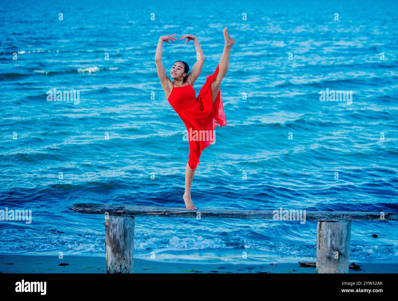 A dancer in a striking red dress performs a ballet pose on a wooden ...
