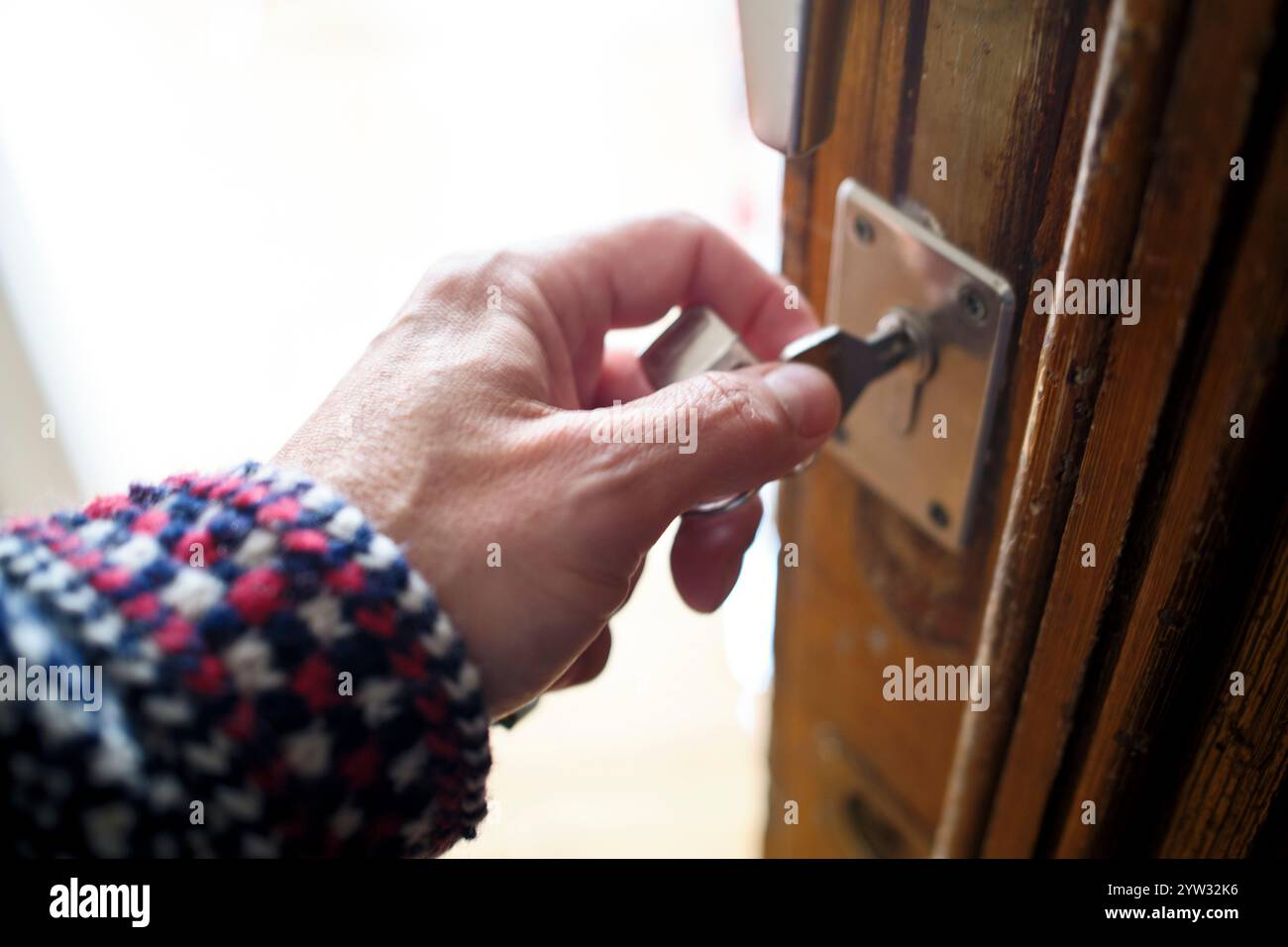 Close-up of a person's hand inserting a key into a wooden door lock ...
