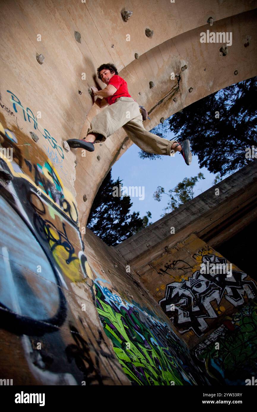 Young climber bouldering below an urban bridge setting surrounded by ...