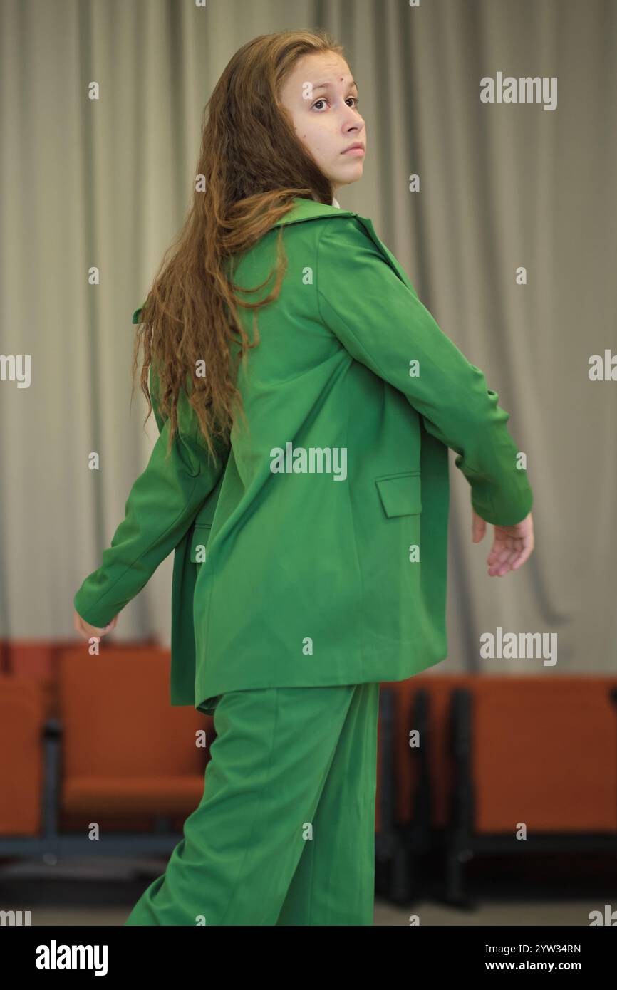A confident young woman draped in a green jacket, looking upward with a thoughtful expression ...