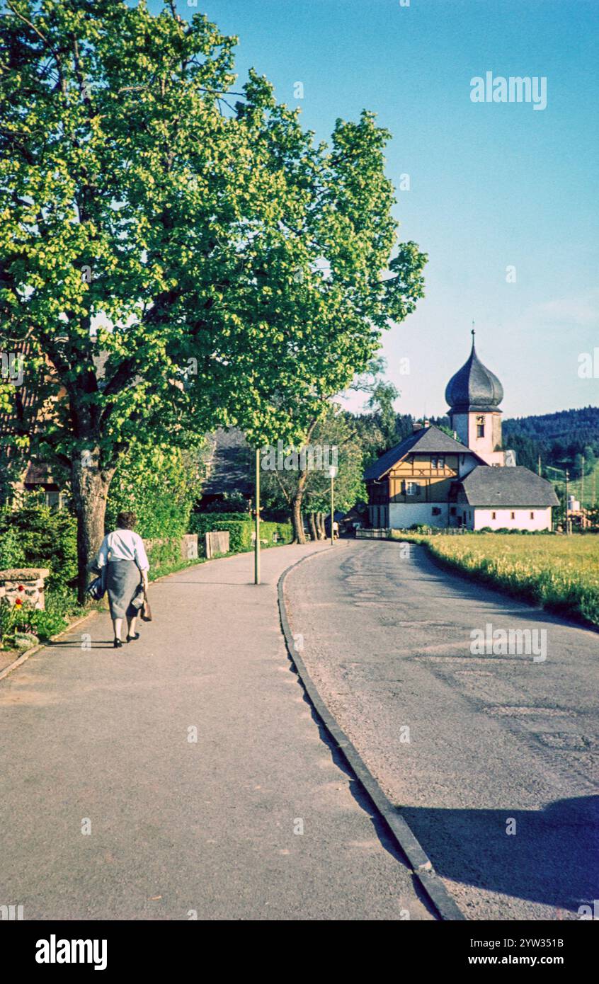 Woman walking along street pavement towards church in village of ...