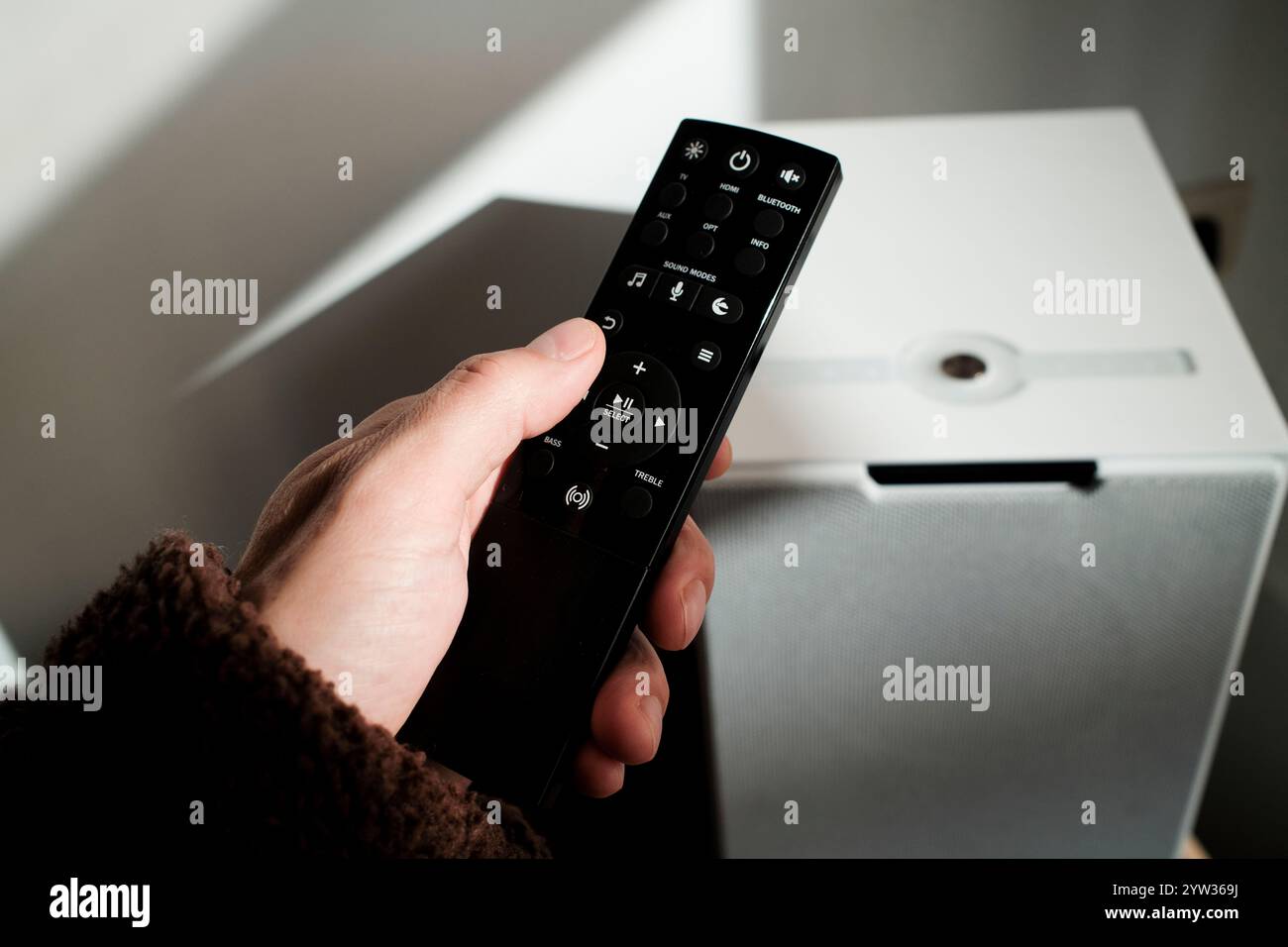 Close-up of a hand holding a black remote control, pointing towards a ...