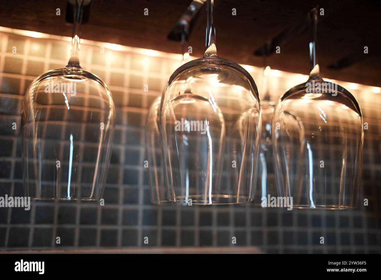 Wine glasses hanging upside down above a bar counter with a warm, dimly ...