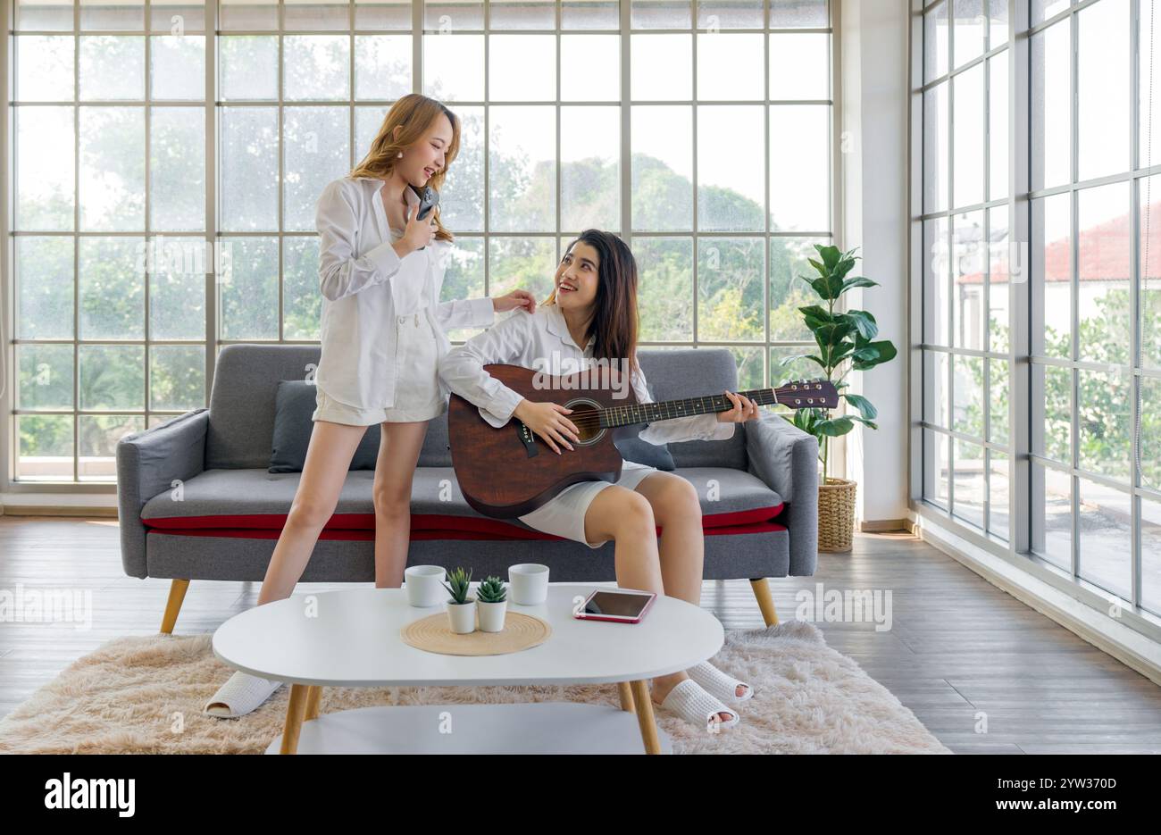 Two friend sit on sofa in a bright living room with large glass wall ...