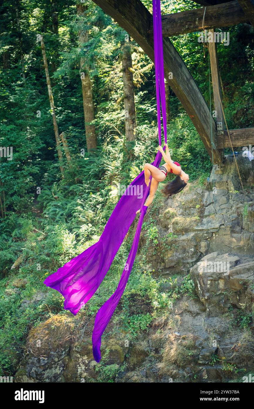 Aerial performer on purple silk ribbons hung under a bridge showcases her flexibility and ...
