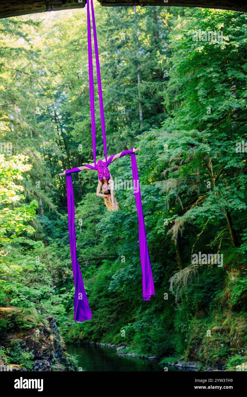 Aerial silk performer hanging from vibrant purple fabric under a bridge ...