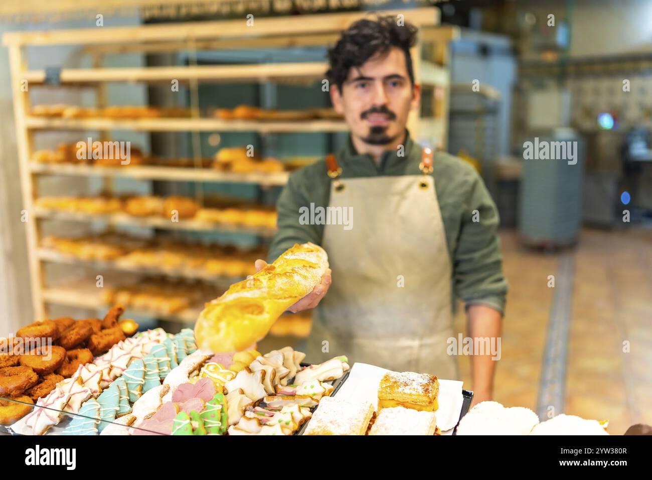 Latin salesman offering an artisan baguette in the bakery shop Stock ...