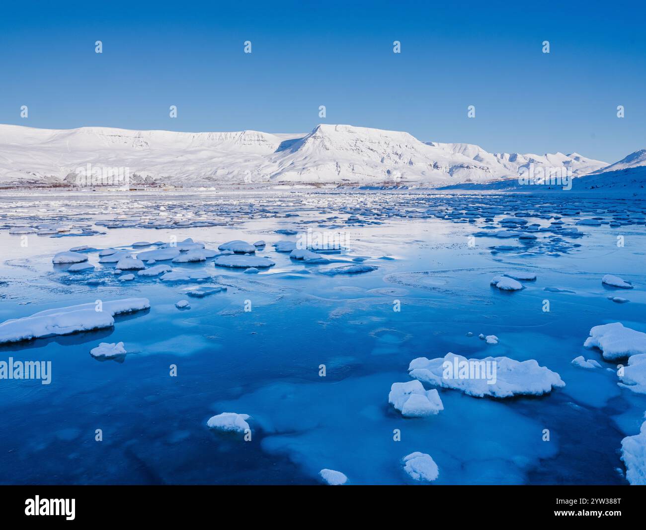 Frozen bay with snow-covered mountains under clear blue skies in Stock ...