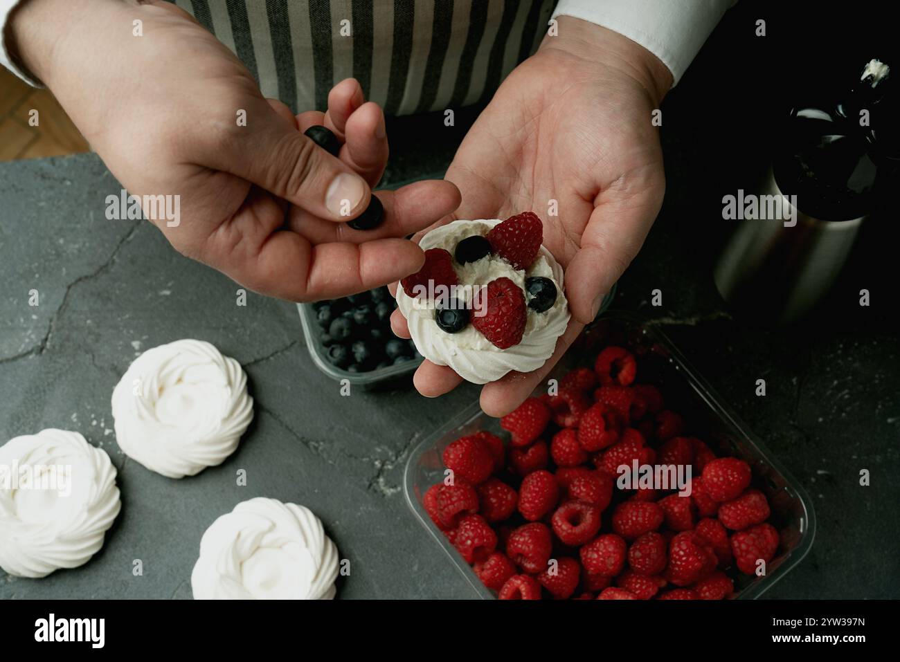 Hand assembling a meringue dessert with raspberries and blueberries ...