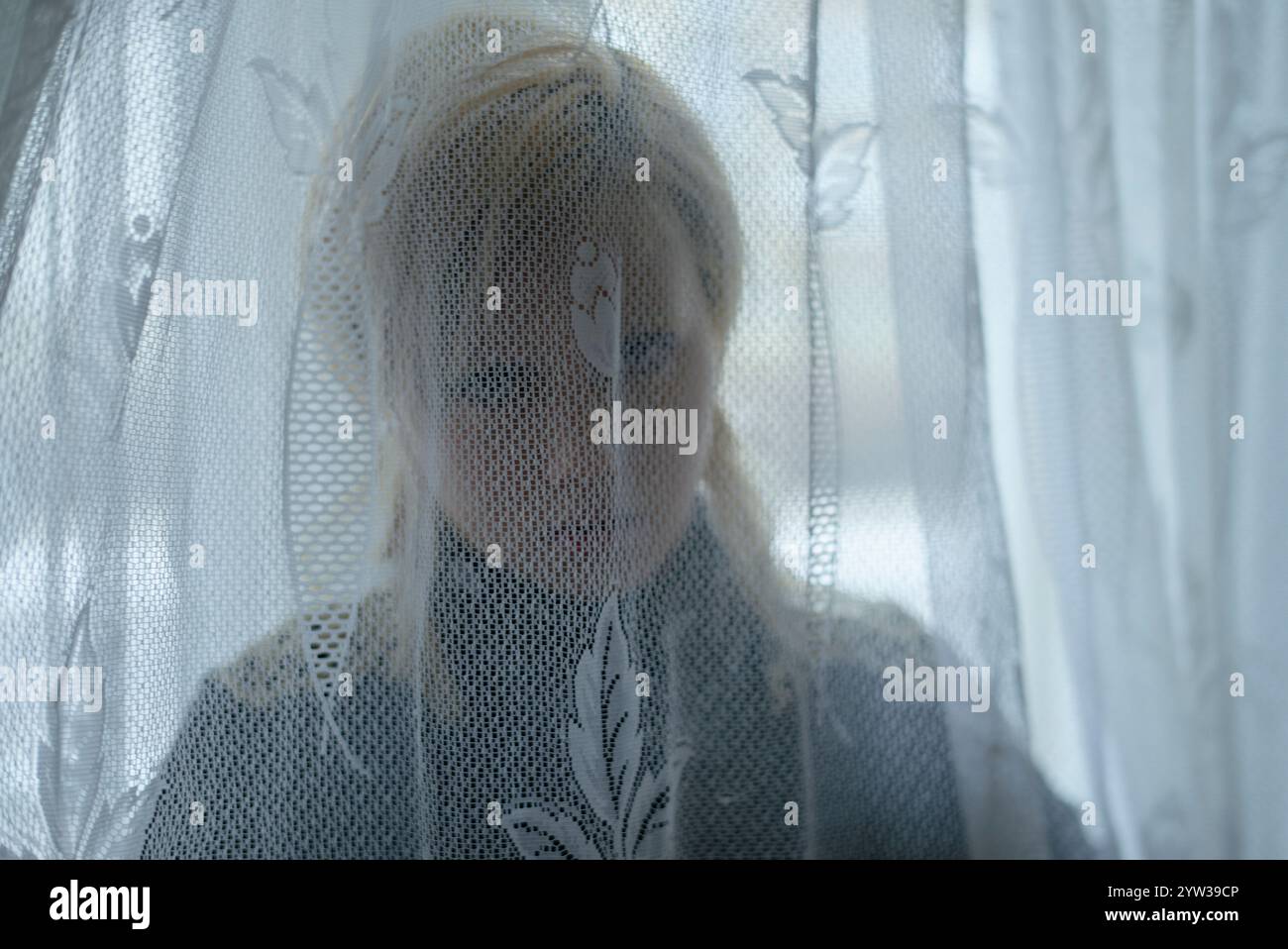 Woman's face partially visible behind a sheer patterned curtain, East ...