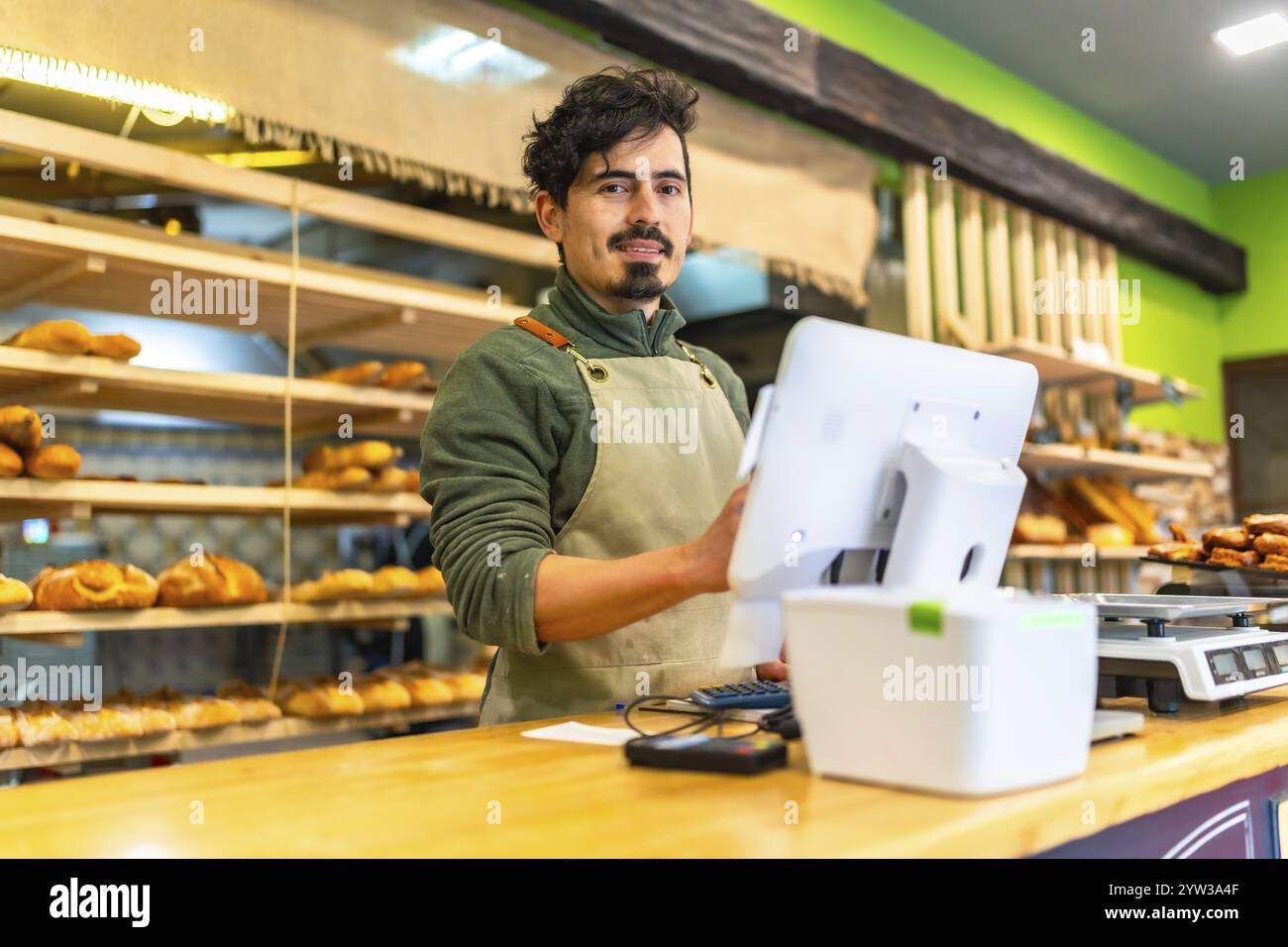 Latin friendly salesman in apron using computer stranding in the ...