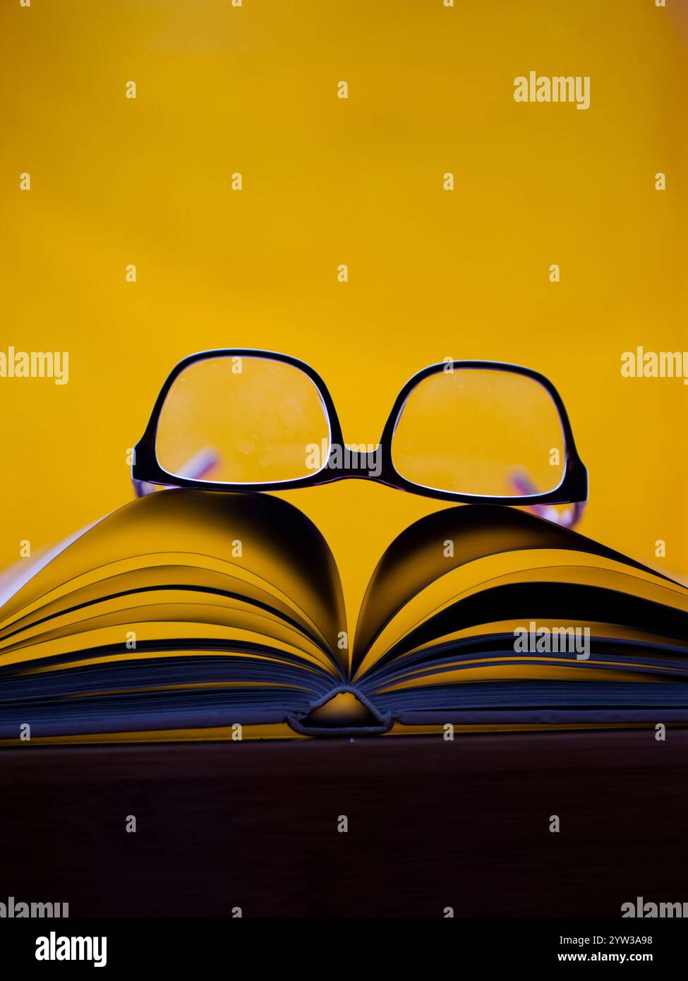 Reading Glasses on Top of an Open Book - Yellow Background Stock Photo ...