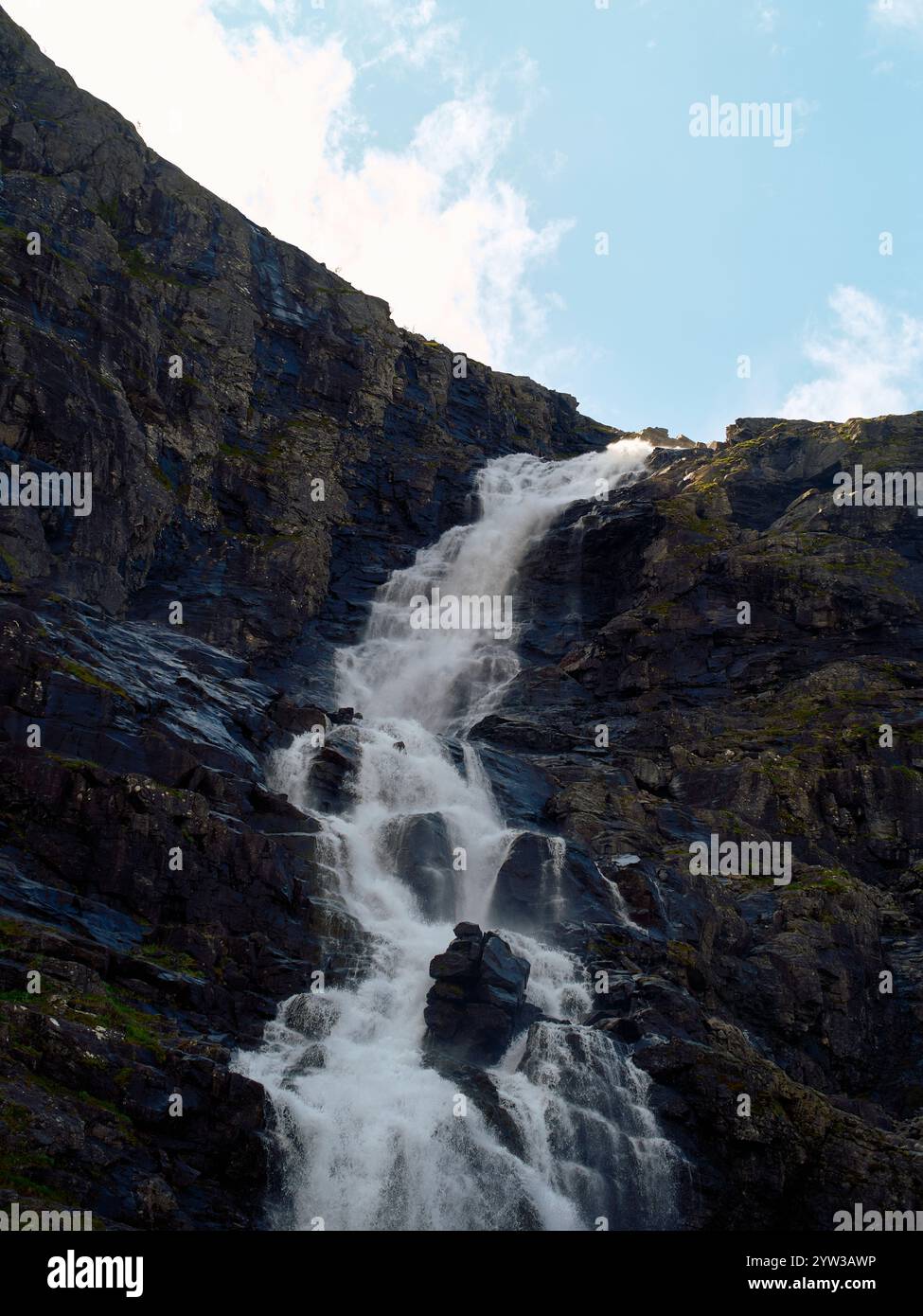 A cascading waterfall flows down a rugged cliff face against a bright ...