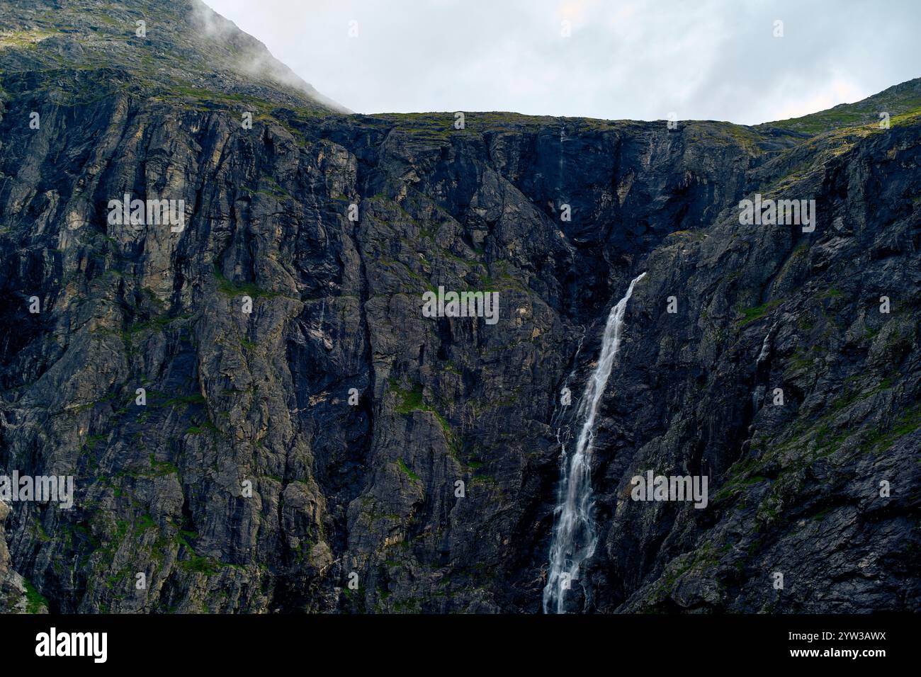 Waterfall cascading down a rugged mountain cliff amidst lush greenery ...