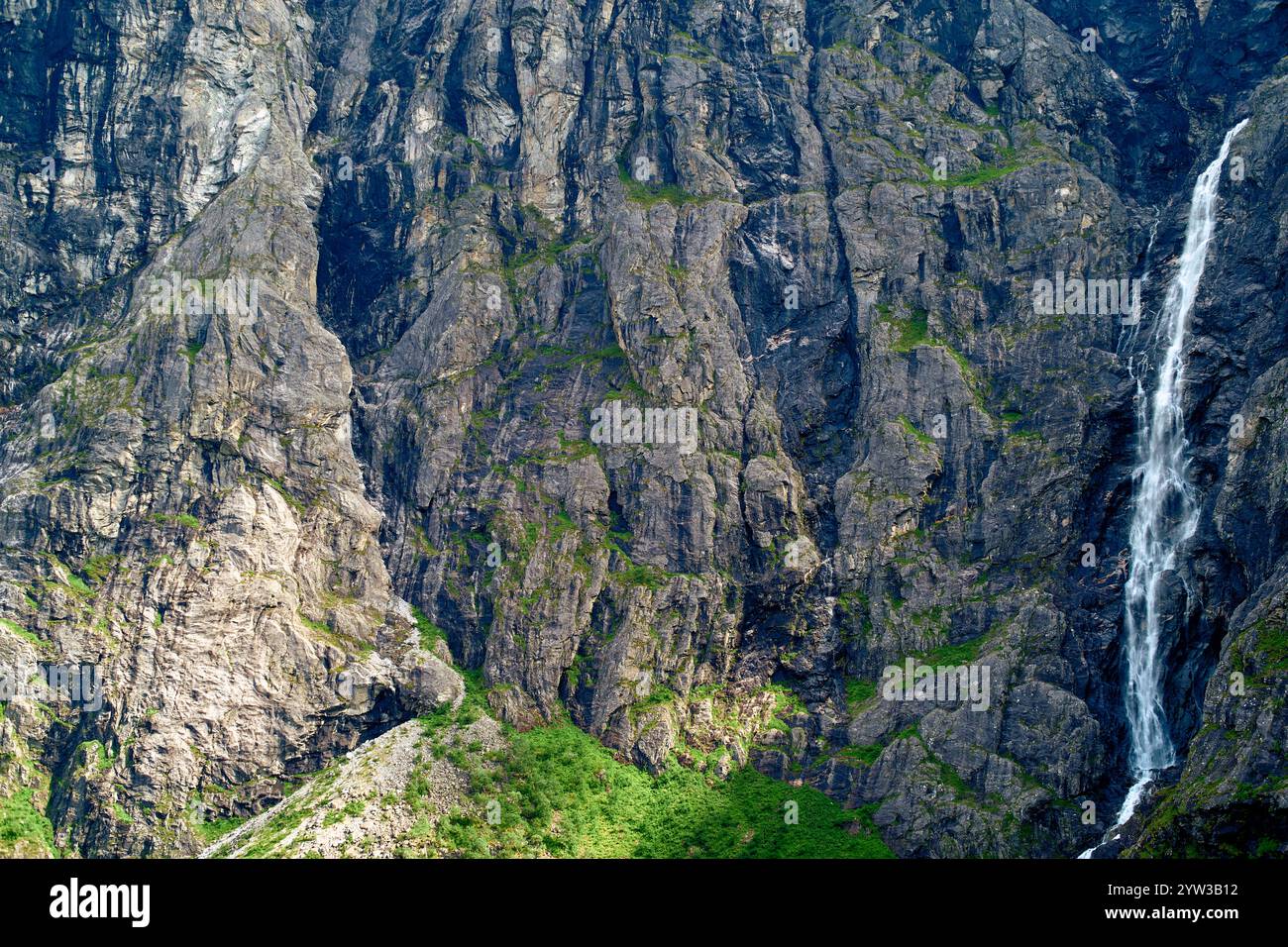 Waterfall cascading down a rugged mountain cliff amidst lush greenery ...