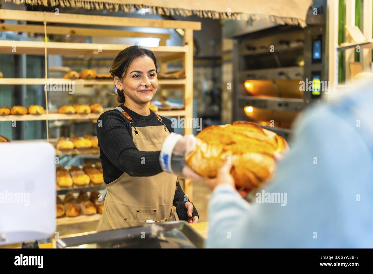 Latin smiling woman selling bread to a client in an artisan bakery ...