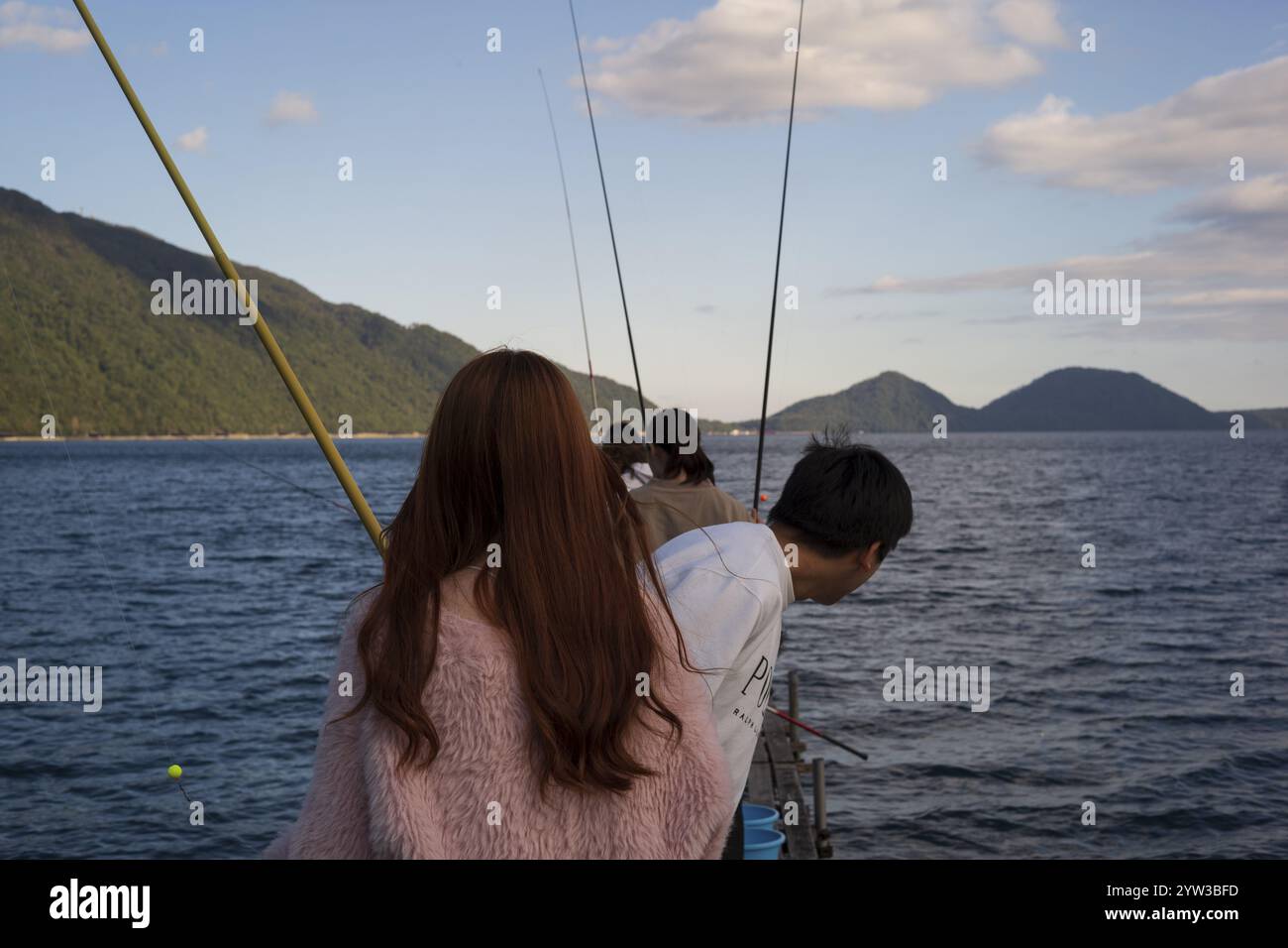 Girl with red hair and pink jacket, fishermen with fishing rods on a ...