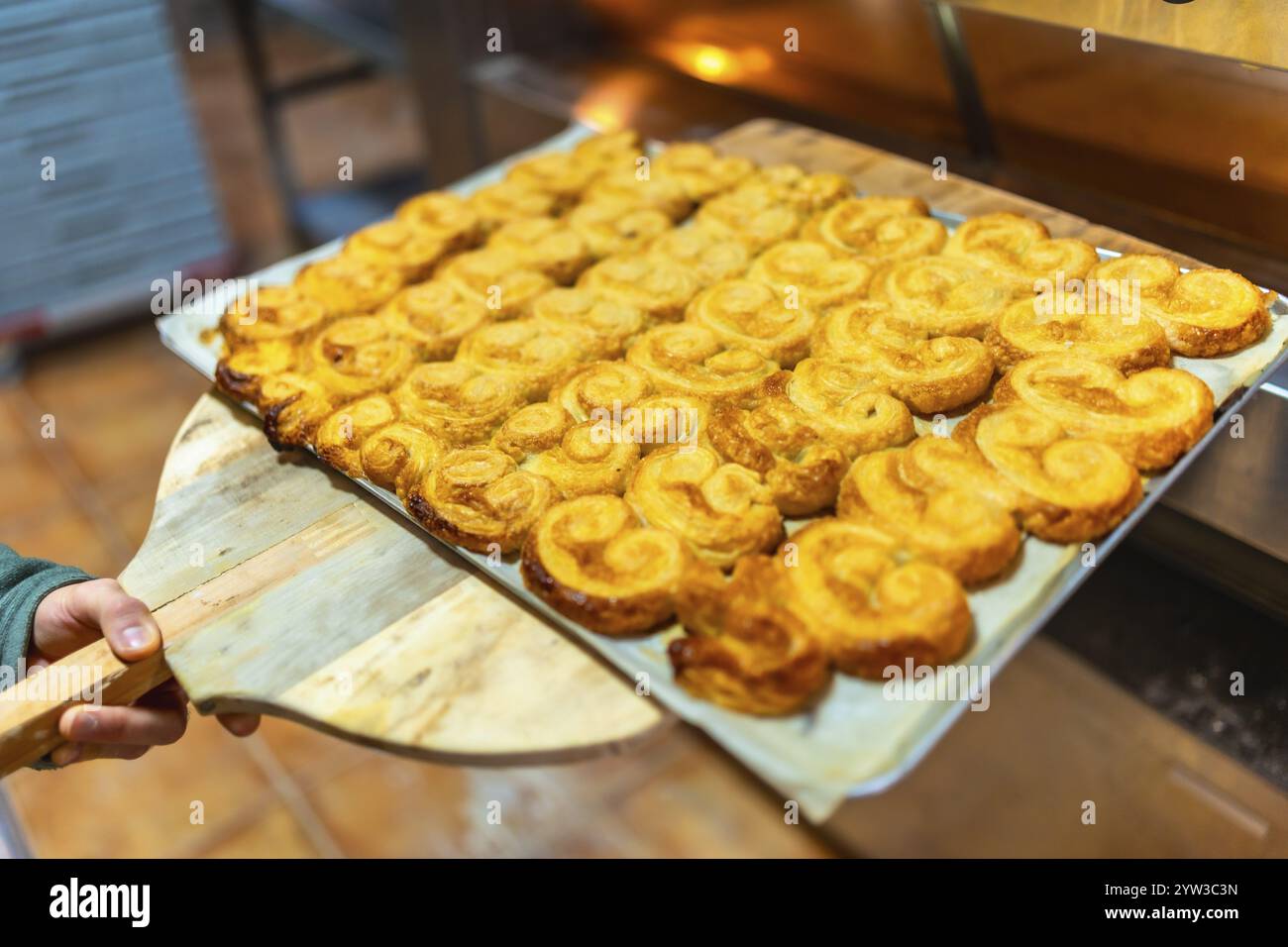 Close-up of a male baker removing artisan baked puff pastry palms from ...
