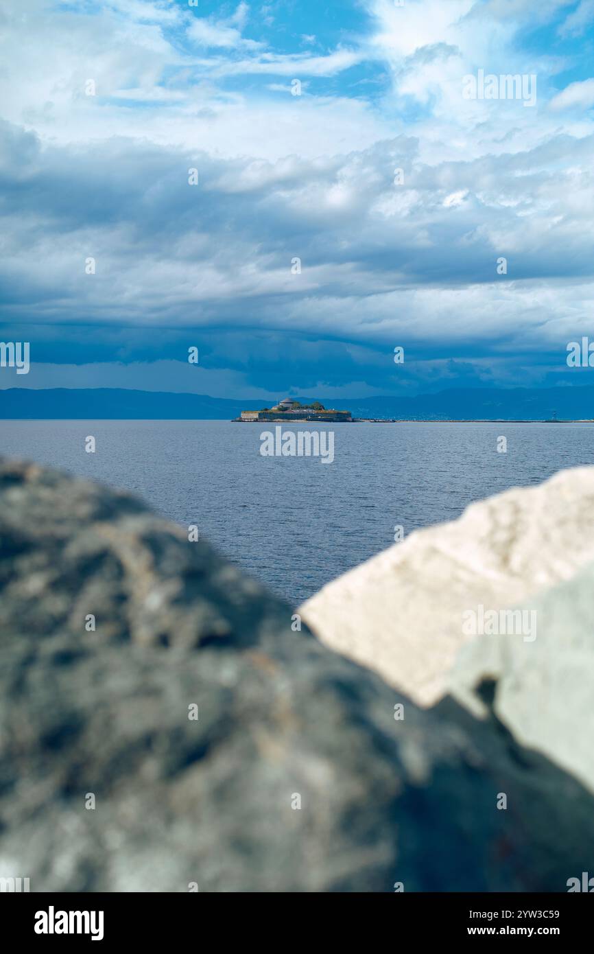 A scenic view of a distant island in the sea under a cloudy sky, with a ...