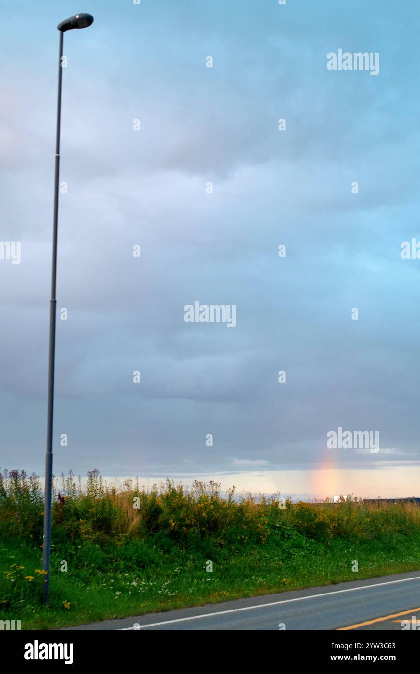 A street lamp stands tall on the side of a road with a rainbow ...