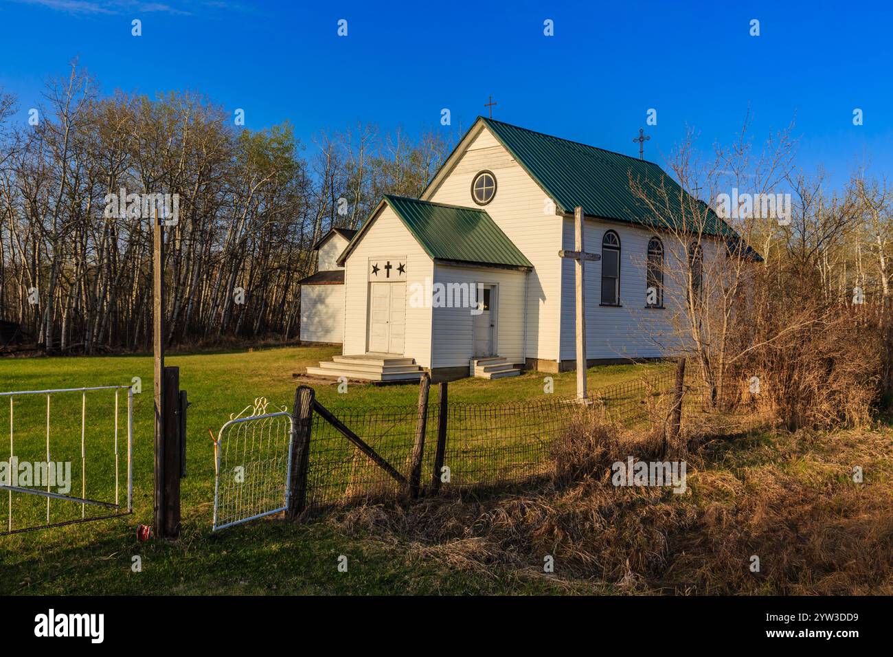 A small white church with a green roof sits in a field. The church is ...