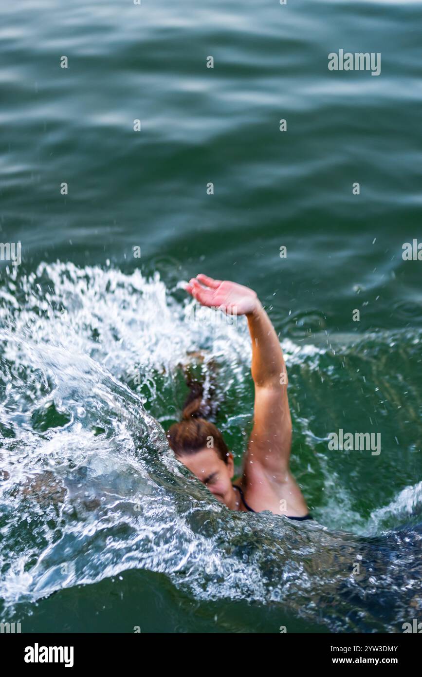 Woman swimming energetically in open water with splashing waves around ...